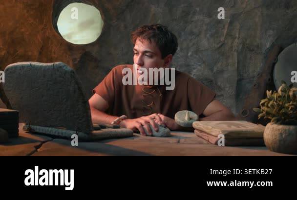 Humorous medium shot of a prehistoric caveman using a stone mouse and ...