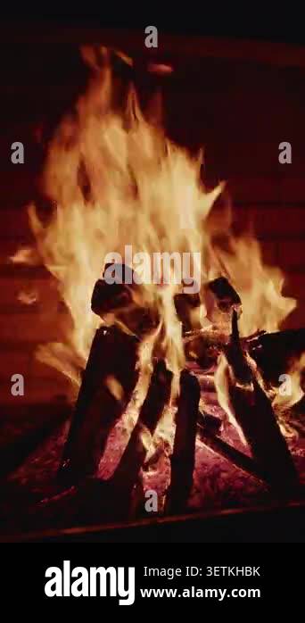A cozy burning bonfire with bright orange flames and glowing logs ...