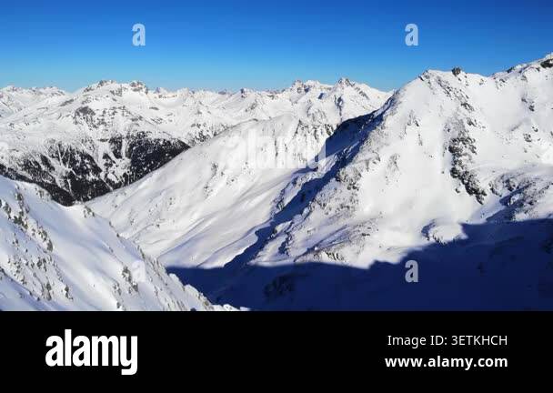 Wide alpine landscape with sunlit snowy peaks, deep valley shadows ...