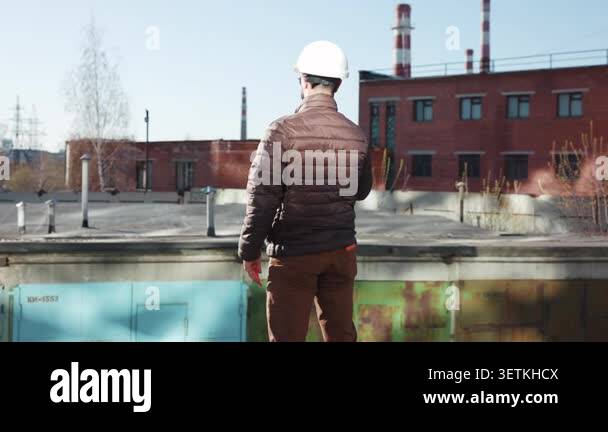 A man seen from behind stands on a rooftop at an industrial facility ...
