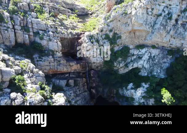 Steep rock formations with dark cave openings, a small waterfall ...