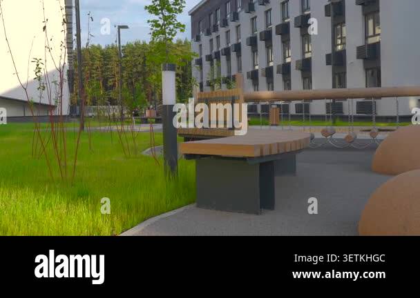 A modern residential courtyard with wooden benches, grass, young trees ...