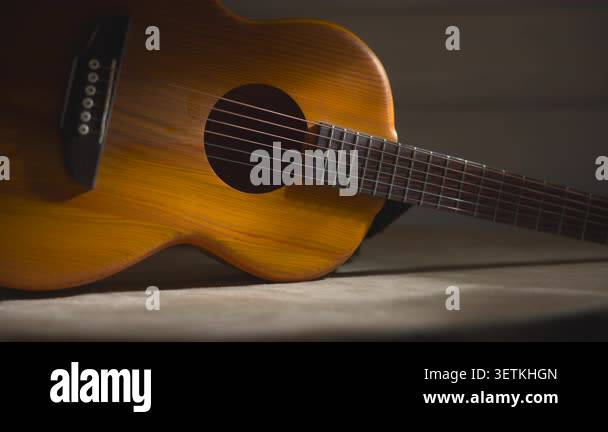 Warm close-up of an acoustic guitar body and fretboard resting on a ...