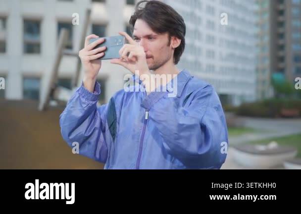Adult man in a blue jacket stands outdoors holding a smartphone ...