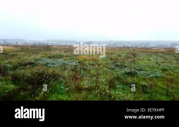 Wide green meadow with wet wild grass in the foreground, a low village ...