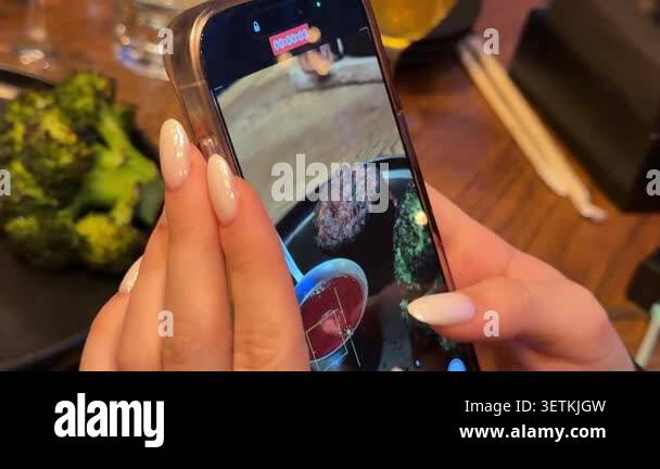 Female hands with white manicure record a plated steak dish on a ...