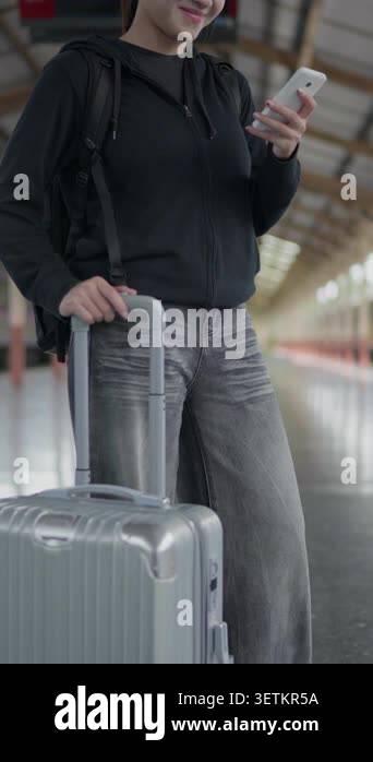 Woman holding suitcase and using smartphone while standing on train ...