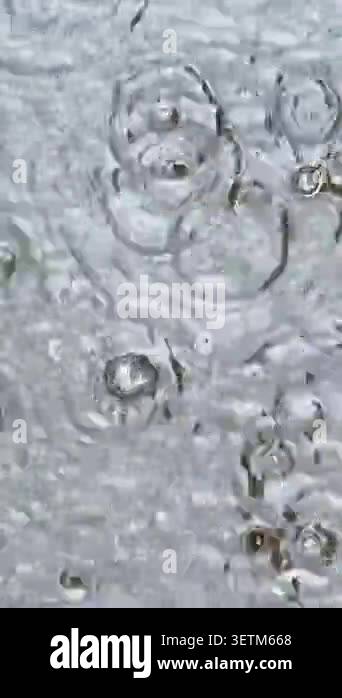 Raindrops falling into water and a puddle, creating circular ripples ...