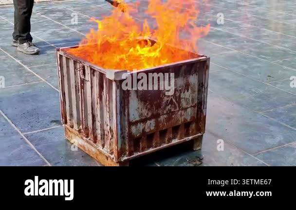 A metal burn container blazes with intense orange flames rising high ...