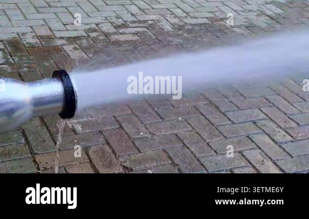 A close-up of a hose nozzle forcefully spraying a dense stream of water ...