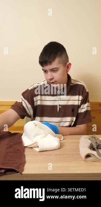 Teenager wearing gloves polishes cutlery with a towel at a table ...