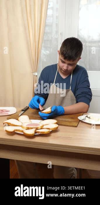 Teenager prepares sausage sandwiches at a kitchen table, carefully ...