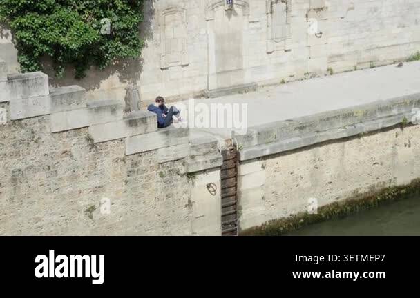 Man sits on a massive historic stone embankment in Paris holding ...