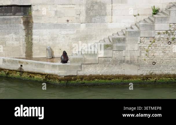 Lonely woman sits by stone stairs on urban river bank. This conceptual ...