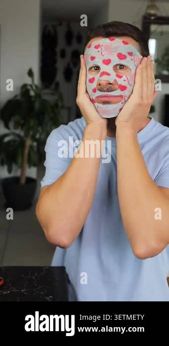 Man applying a heart-patterned face mask, holding it in place with his ...