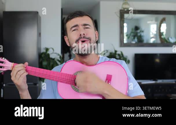 A man is playing a pink guitar and singing, looking directly at the ...