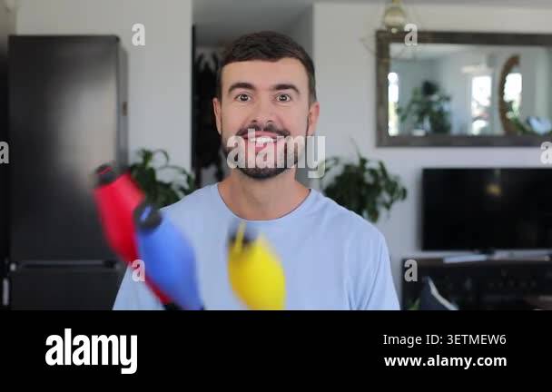 Man with a beard is juggling three colorful pins, looking surprised and ...