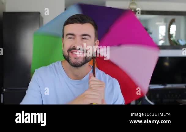 A man with a beard is holding a colorful umbrella and smiling, looking ...