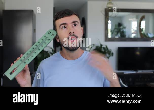 Man holding a thermometer to his head, fanning himself, looking ...