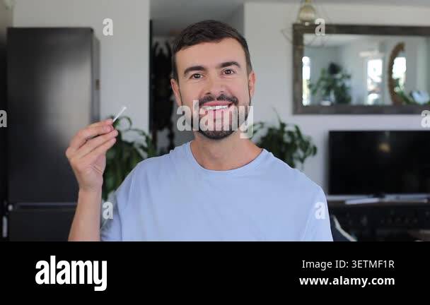 A man is cleaning his ear with a cotton swab in a well-lit room. He ...
