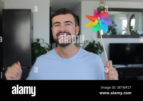 A man is holding a colorful pinwheel and smiling at the camera, indoors ...