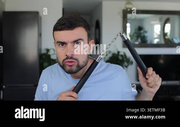 A man with a beard and intense expression is practicing with nunchucks ...