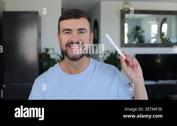 A man in a light blue t-shirt holds a pregnancy test and its cap ...