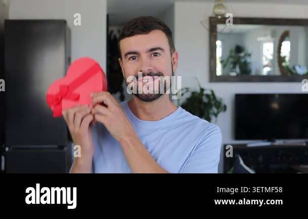 A man playfully holds a red heart-shaped gift box, making various ...