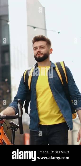 A smiling food delivery man enjoys his day while riding his bicycle in ...