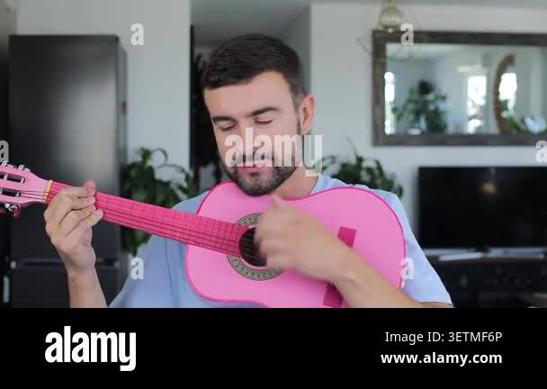 A man is playing a pink guitar and singing, looking at the camera in a ...