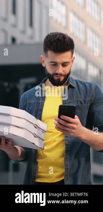 A delivery man in a yellow shirt holds pizza boxes and dials a number ...