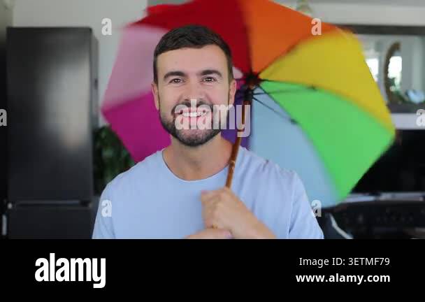 A man with a rainbow umbrella is spinning it around and smiling at the ...