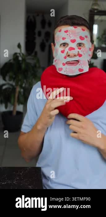 Vertical video showing a man wearing a heart-patterned face mask holds ...