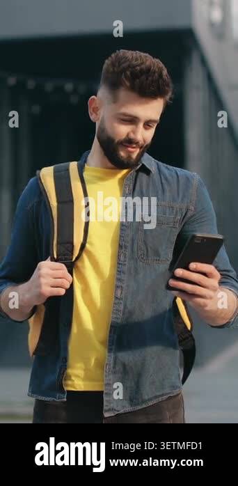 A food delivery man stands with a backpack, focused on his phone ...