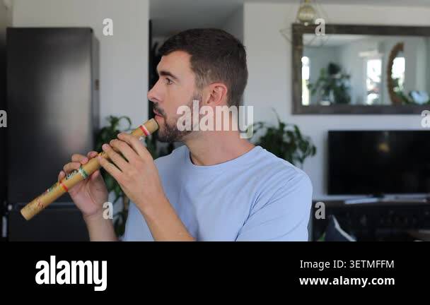 A man playing a wooden flute indoors, with plants and a mirror in the ...