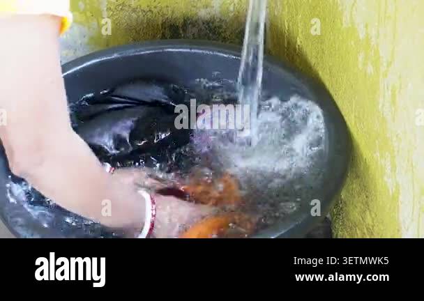 A woman hand washing clothes in a black plastic basin with water ...