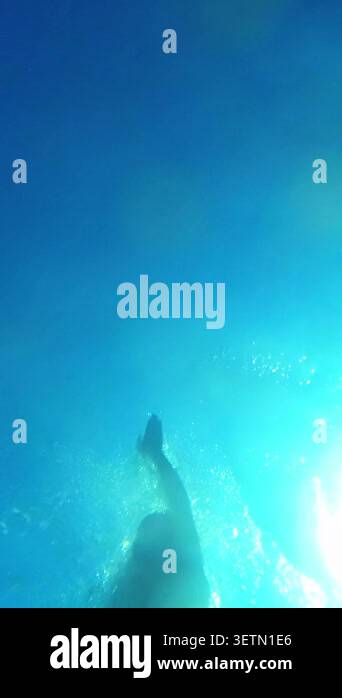 Man swimming in clear blue ocean water with bright sun rays seen from ...