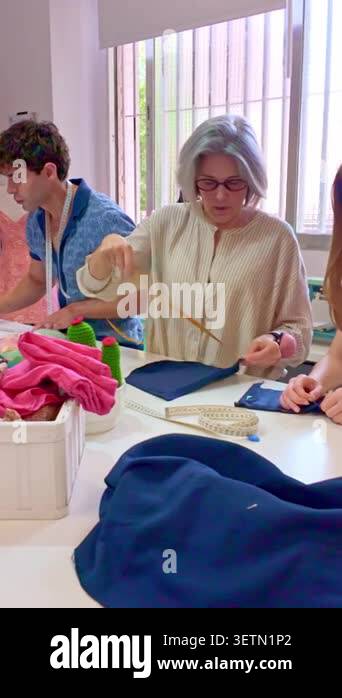 Senior instructor guiding young students during a tailoring class in a ...