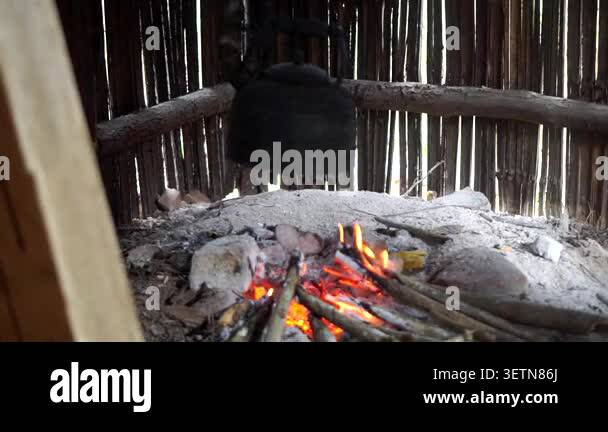 A traditional soot-covered black kettle suspended over campfire embers ...