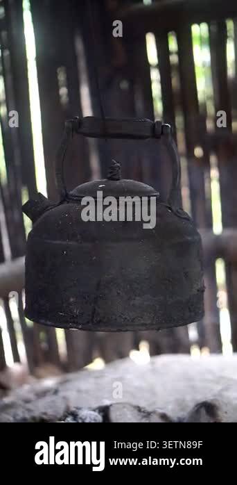 A traditional soot-covered black kettle suspended over campfire embers ...