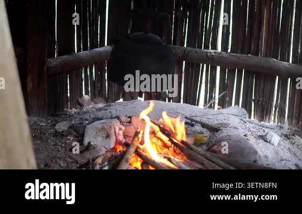 A traditional soot-covered black kettle suspended over campfire embers ...