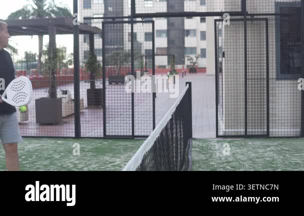 A large man plays padel through the net in his yard in the summer in ...