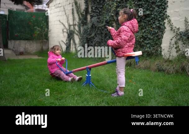 Two little sisters enjoy playing together on a seesaw in the backyard ...