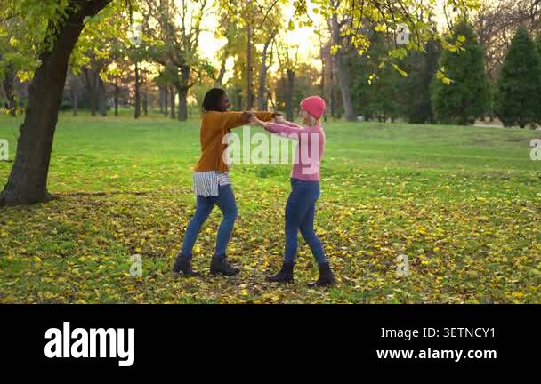 Two cheerful young women holding hands and dancing together in a park ...