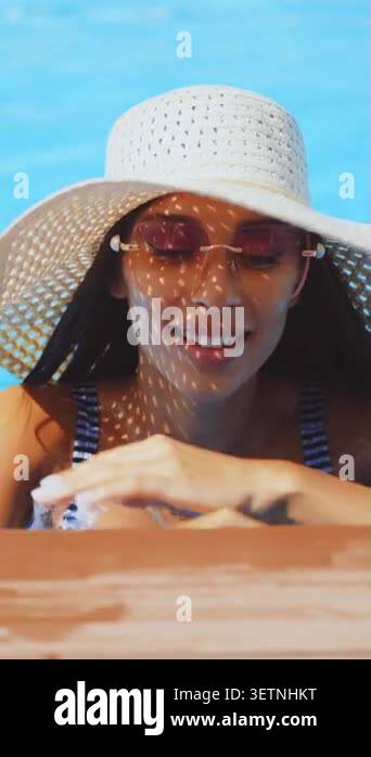 Beautiful young woman in straw hat and sunglasses smiling by pool ...