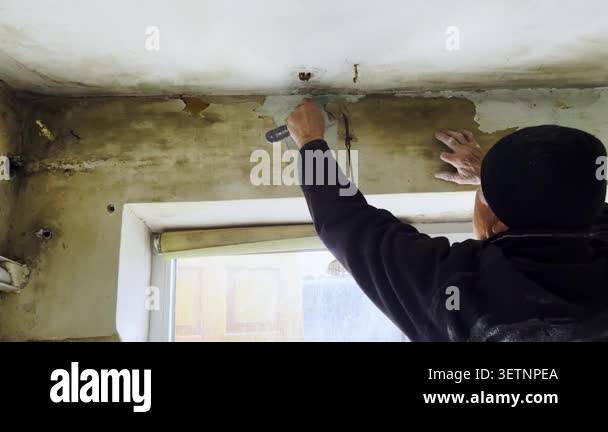 Male hands use putty knife to scrape and remove old plaster from an ...
