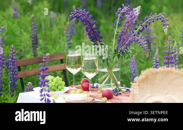 Table setting with wine glasses and fruit surrounded by lupine flowers ...