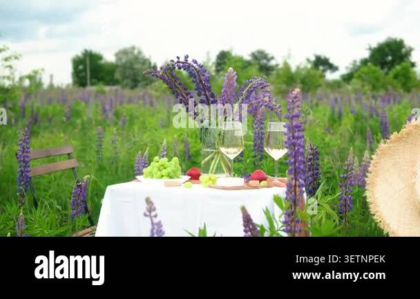 Outdoor table setting with wine and fruit in a field of lupine flowers ...