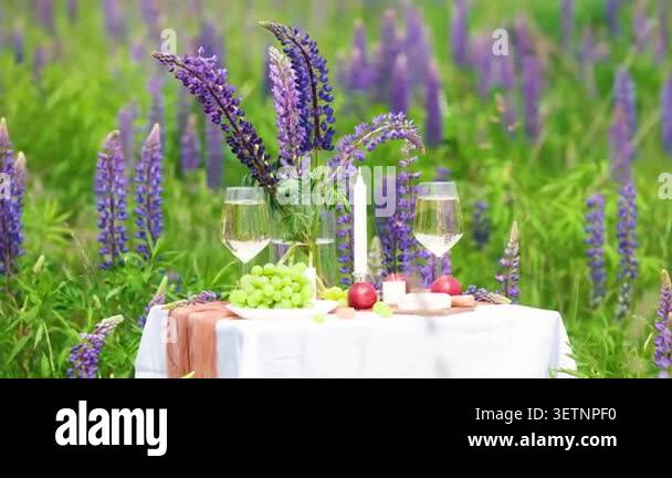 Table with food and wine set among purple lupine flowers in a meadow ...