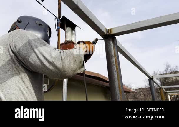 Manual laborer in protective mask weld iron detail on carport frame ...